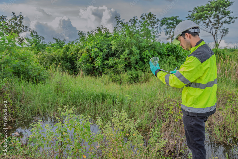 Environmental engineer wearing safety gear collecting water sample from ...
