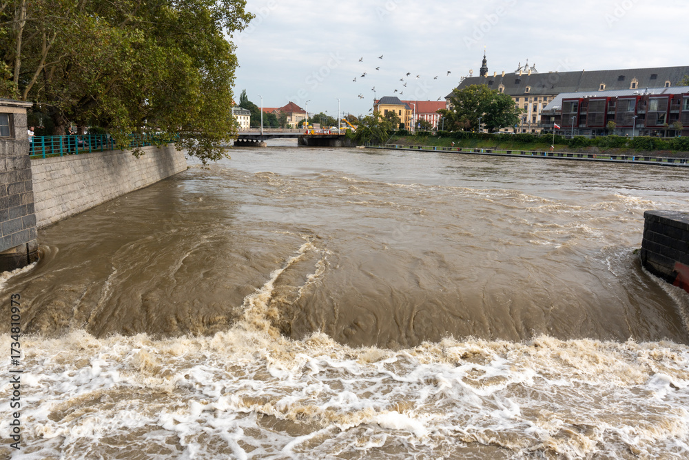 Turbulent muddy flood water rushing through urban river with historic ...