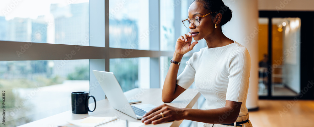 Woman using laptop and thinking while working near large window Stock ...