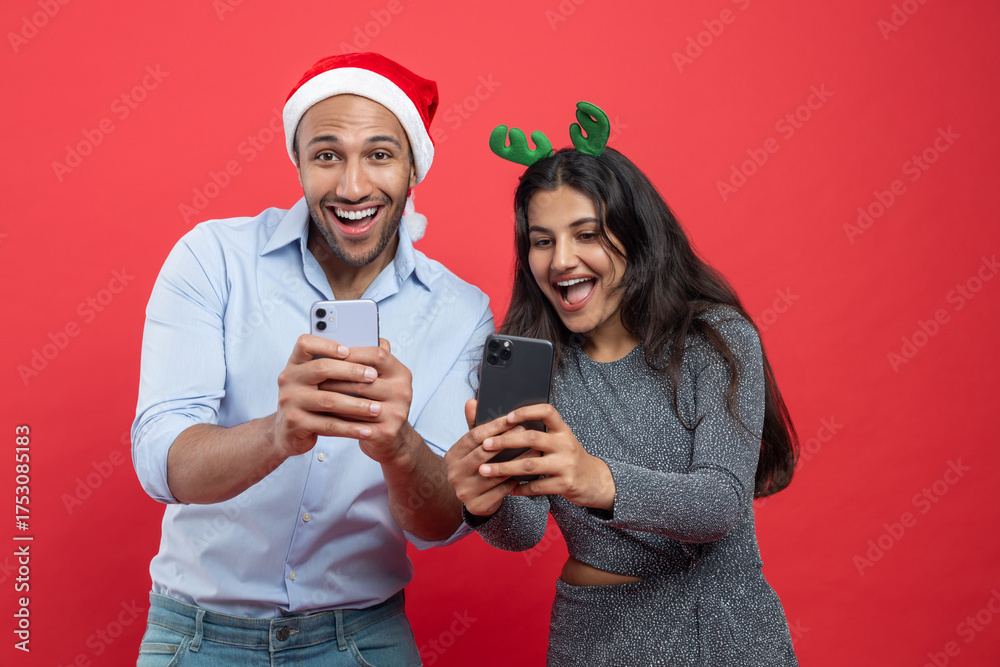 Couple in Santa hats using phones to share holiday greetings and ...