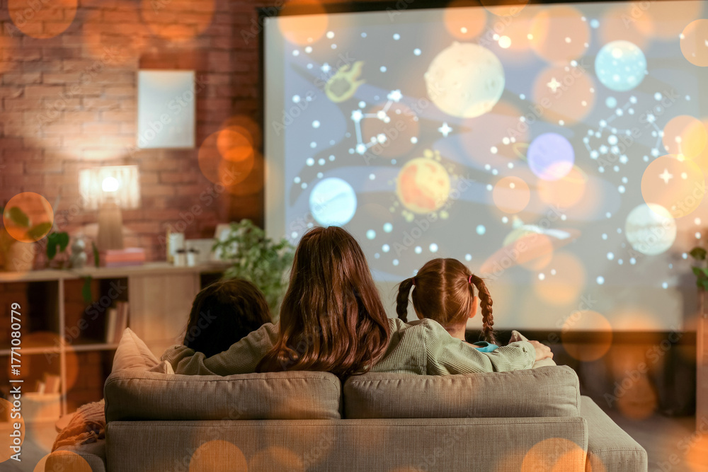 Cute girls with their mother watching cartoons on projector screen at ...