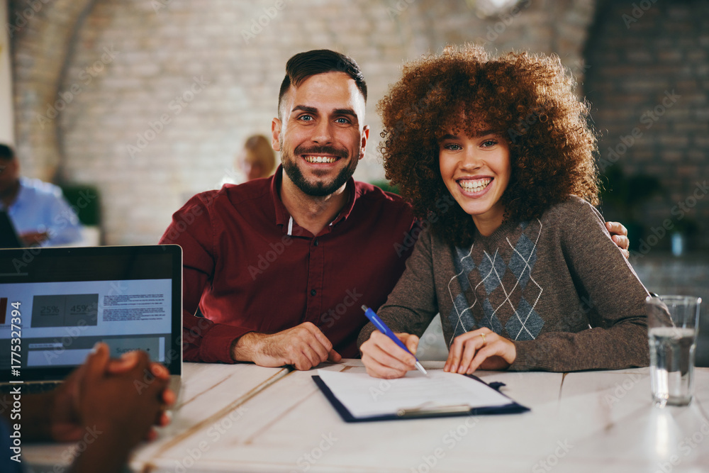Extremely happy couple smiles directly at the camera while signing a ...
