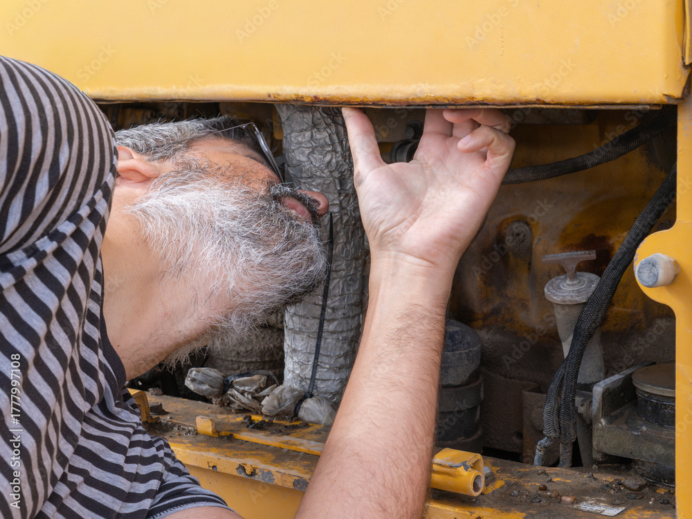 Mechanic troubleshooting a backhoe engine in a heavy equipment ...