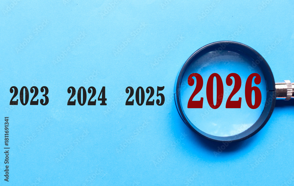 New Year 2026 is enlarged using a magnifying glass on blue background ...