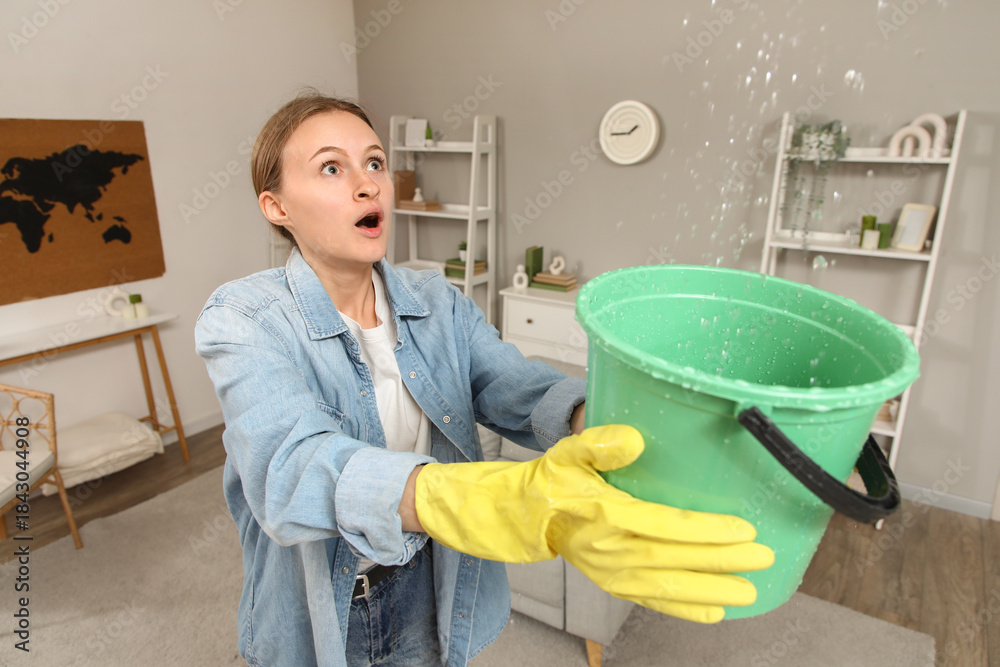 Shocked young woman placing green bucket under water dripping from ...