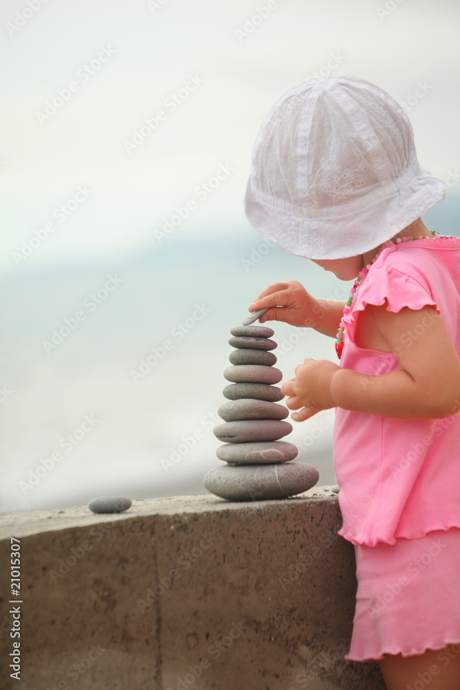 little girl is building a construction from pebble stones. Stock Photo ...