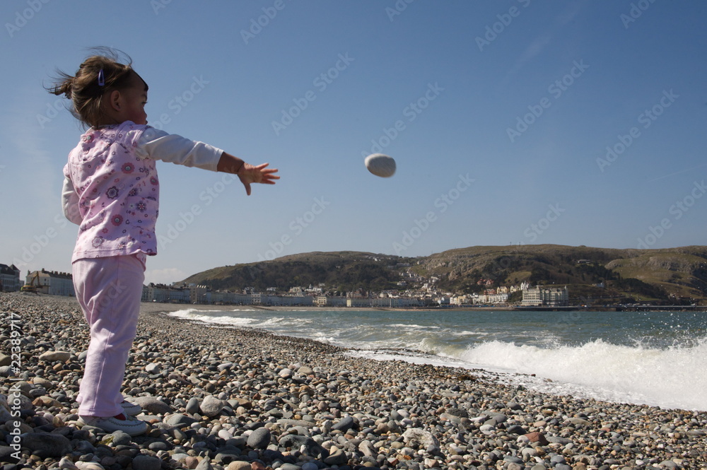 Little girl happily throwing pebbles into the sea Stock Photo | Adobe Stock
