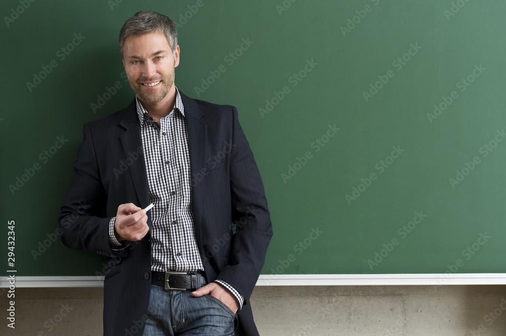 Glücklicher Lehrer steht vor der Tafel und lacht. Stock Photo | Adobe Stock