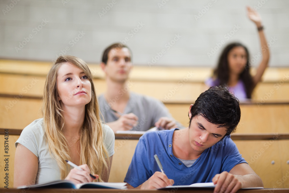 Poster Students taking notes while their classmate is raising her hand ...