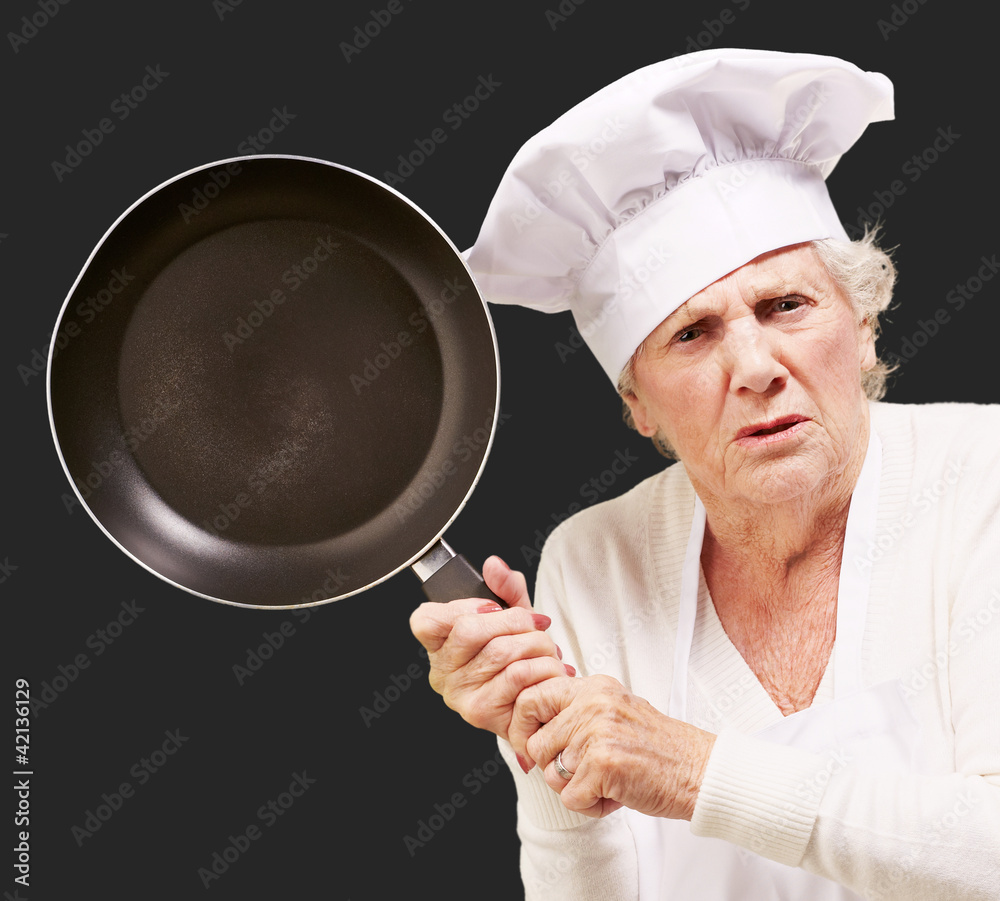 Cook senior woman angry trying to hit with pan over black backgr Stock ...