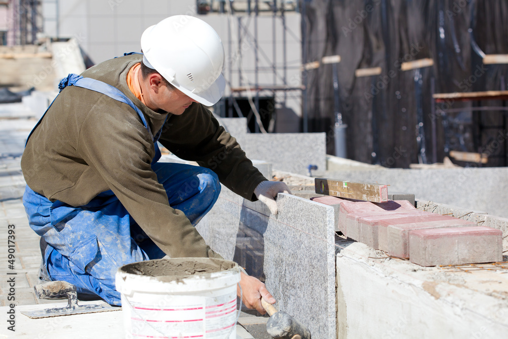 Tiler in helmet and work wear installing marble tiles Stock Photo ...