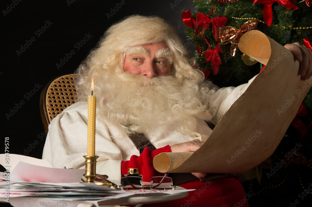 Santa Claus sitting at home and reading old paper roll to do lis Stock ...
