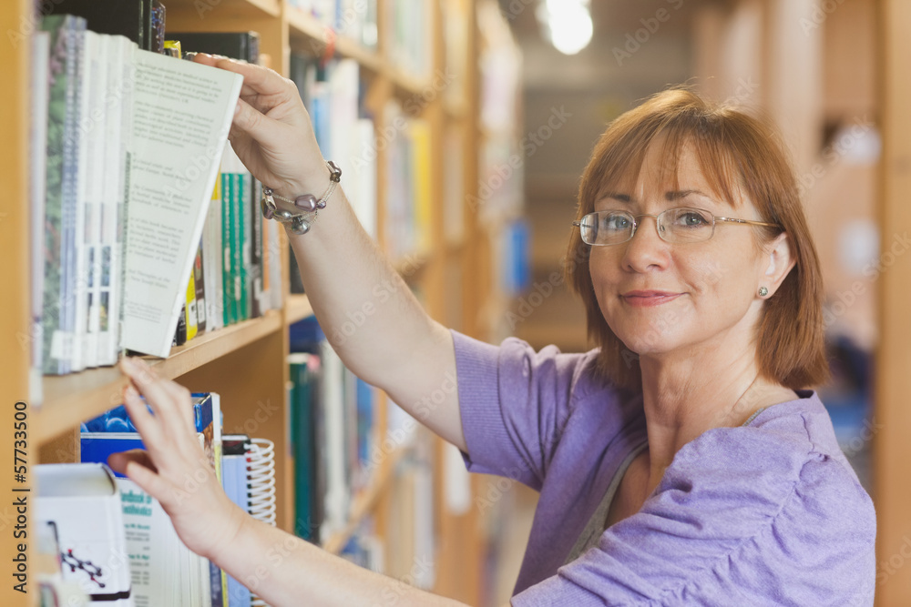 Poster Mature female librarian taking a book off a shelf – Wall Art ...