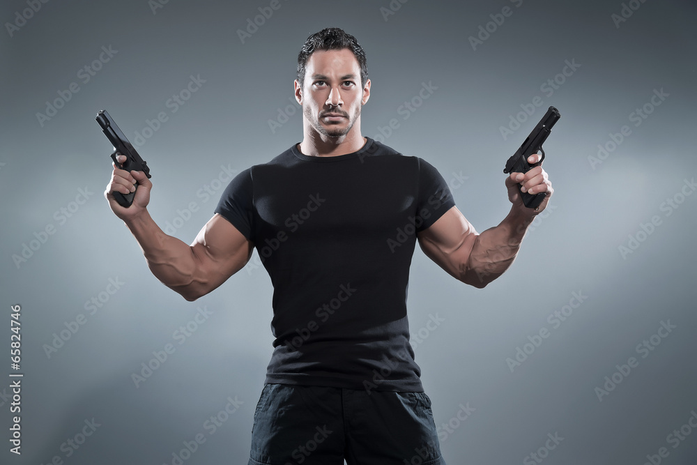 Action hero muscled man holding two guns. Wearing black t-shirt foto de ...