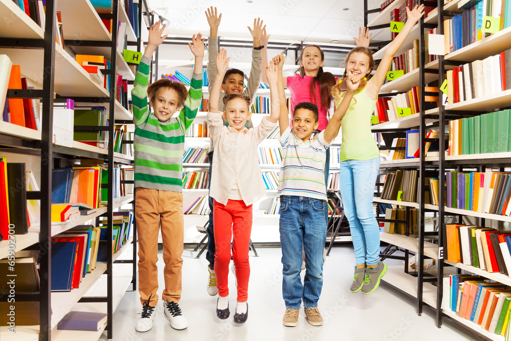 Happy kids jumping with hands up in the library Stock Photo | Adobe Stock