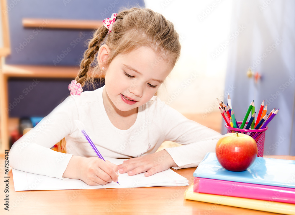 Cute smiling little girl is writing at the desk Stock Photo | Adobe Stock