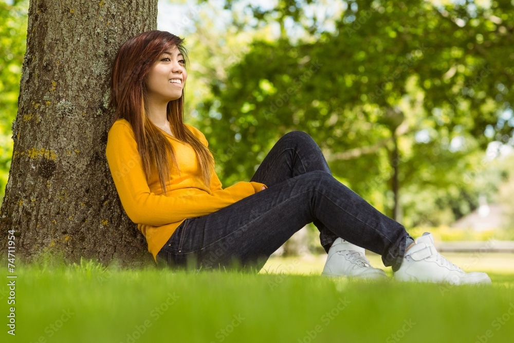Beautiful woman sitting against tree in park Stock Photo | Adobe Stock