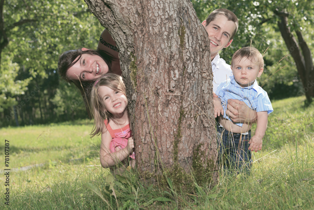 A Smiling family standing behind a tree Stock Photo | Adobe Stock