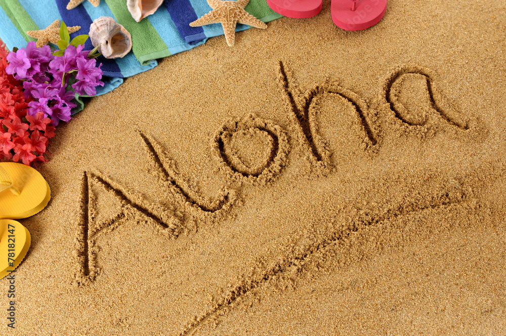 The word Aloha written in sand on a beach with towel flip flops ...