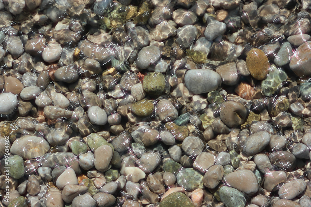 Sea pebbles in water. Ripples on the surface of water and solar patches ...