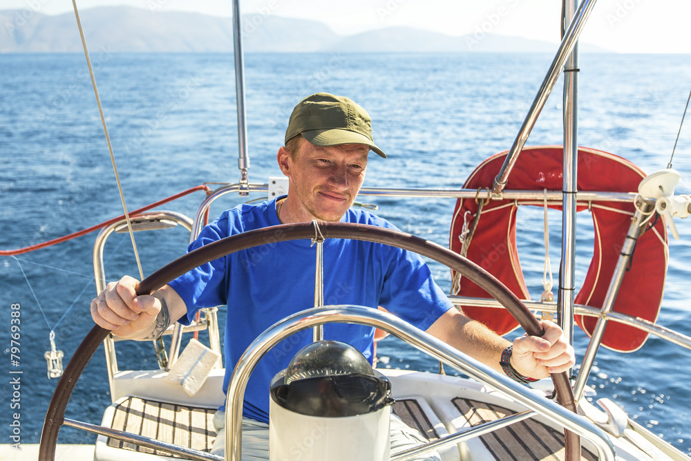 Man skipper at the helm controls sailing yacht. Stock Photo | Adobe Stock