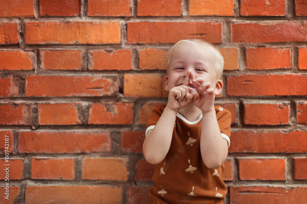Cute little boy making funny faces on a brick wall background Stock ...