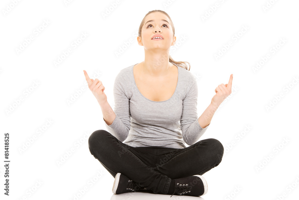 Woman sitting cross legged pointing up. Stock Photo | Adobe Stock