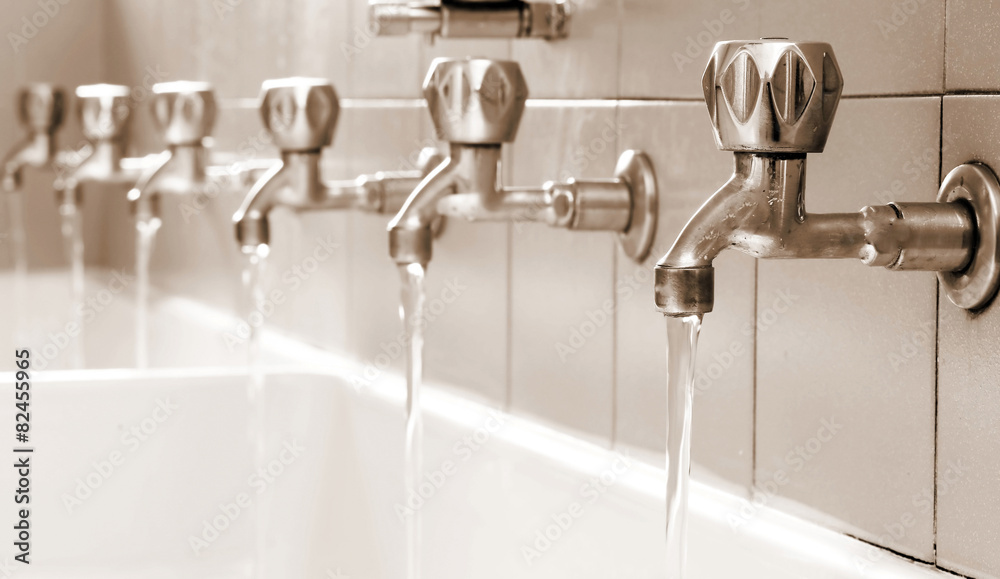 row of steel taps into a large bathroom in the community Stock Photo ...