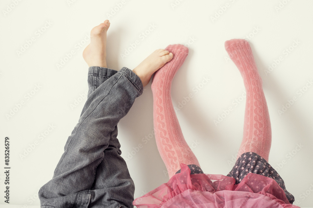 Close-up of a boy and girl lying on the floor with their legs against a ...
