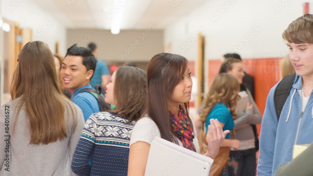 A small group of students stand in a high school hallway and talk to ...
