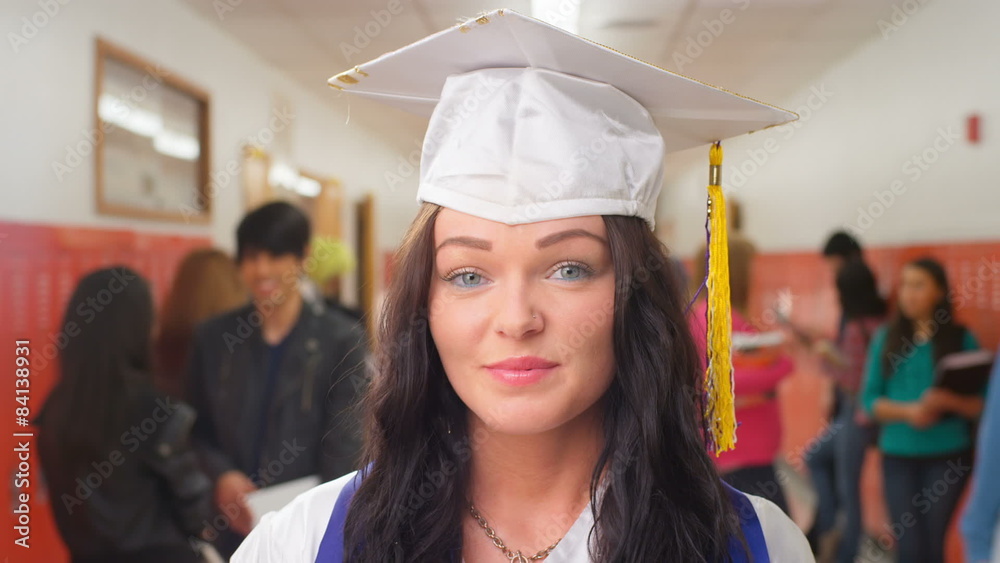 Female student wearing a graduation cap and gown stands in a hallway ...