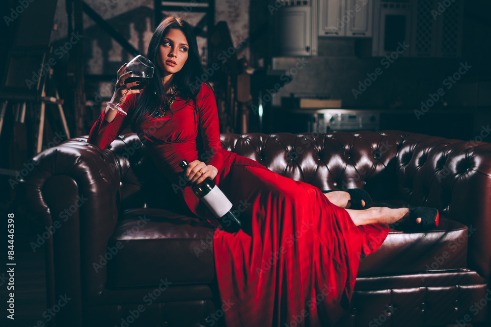 young woman in red dress sitting on leather sofa Stock Photo | Adobe Stock