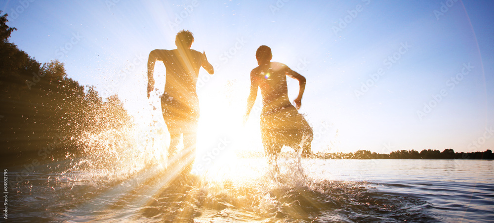 Glückliche junge Menschen laufen und springen am See beim ...