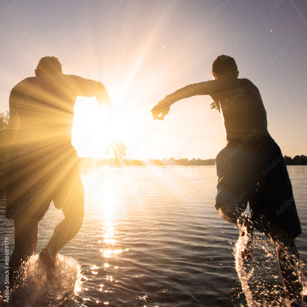 Glückliche junge Menschen laufen und springen am See beim ...