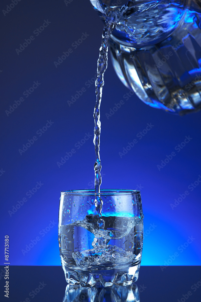 Pitcher water poured into a glass, splash, blue background, refreshing ...