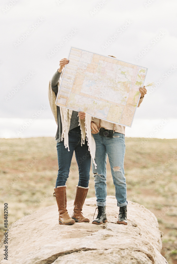 Two women standing holding up a large map in front of their faces ...