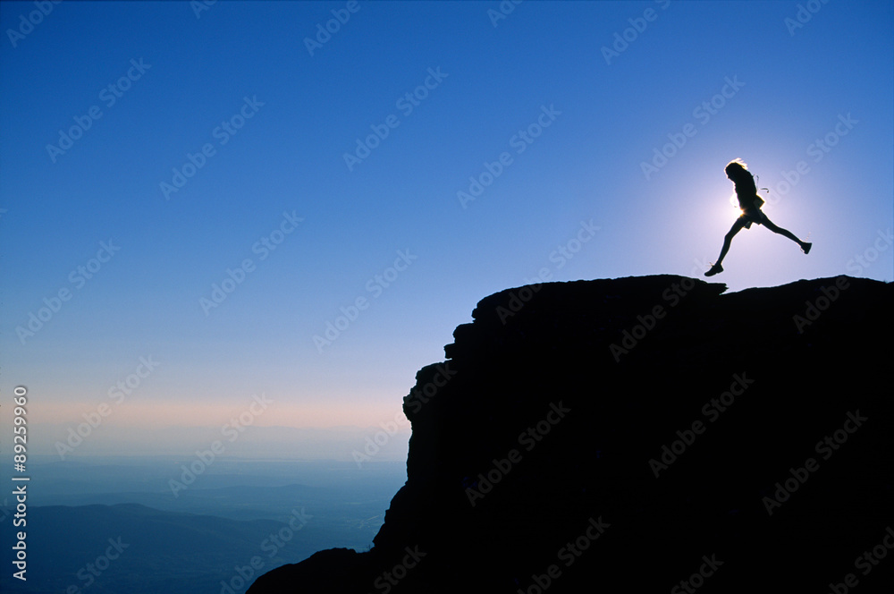 Silhouette of a girl jumping over a rock cliff. Stock Photo | Adobe Stock