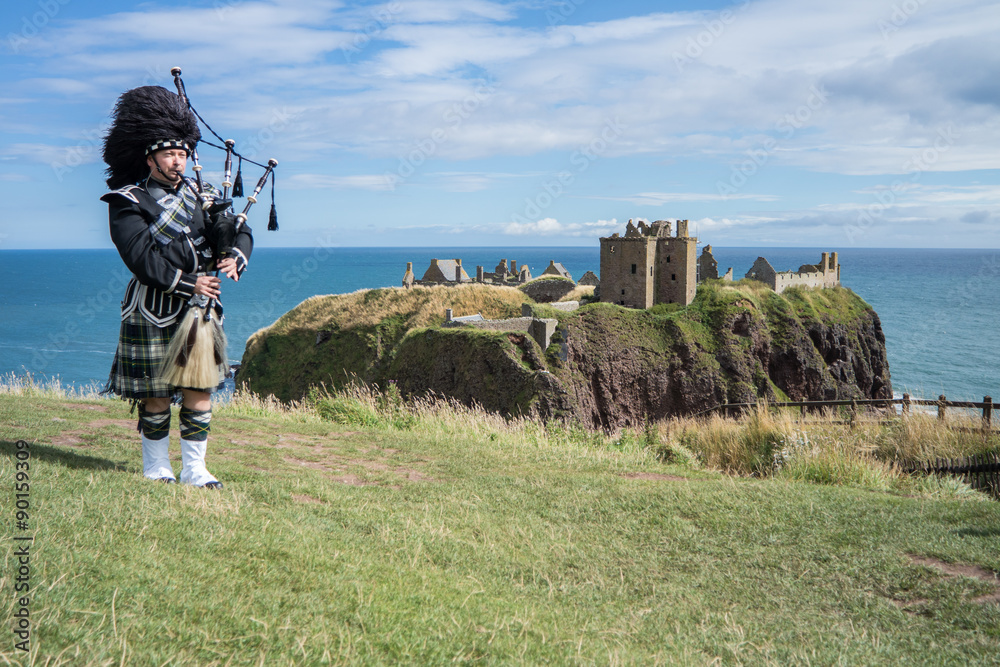 Traditional scottish bagpiper in full dress code at Dunnottar Castle in ...