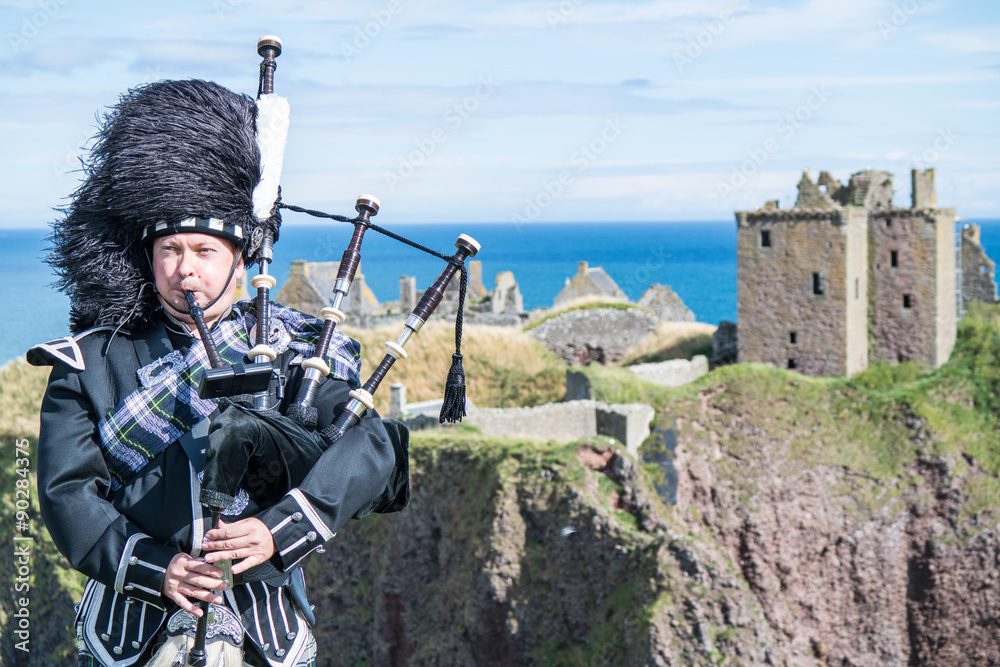 Traditional scottish bagpiper in full dress code at Dunnottar Castle in ...