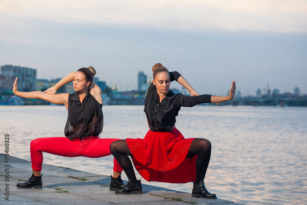 Two young beautiful twin sisters are dancing waacking dance in the city ...