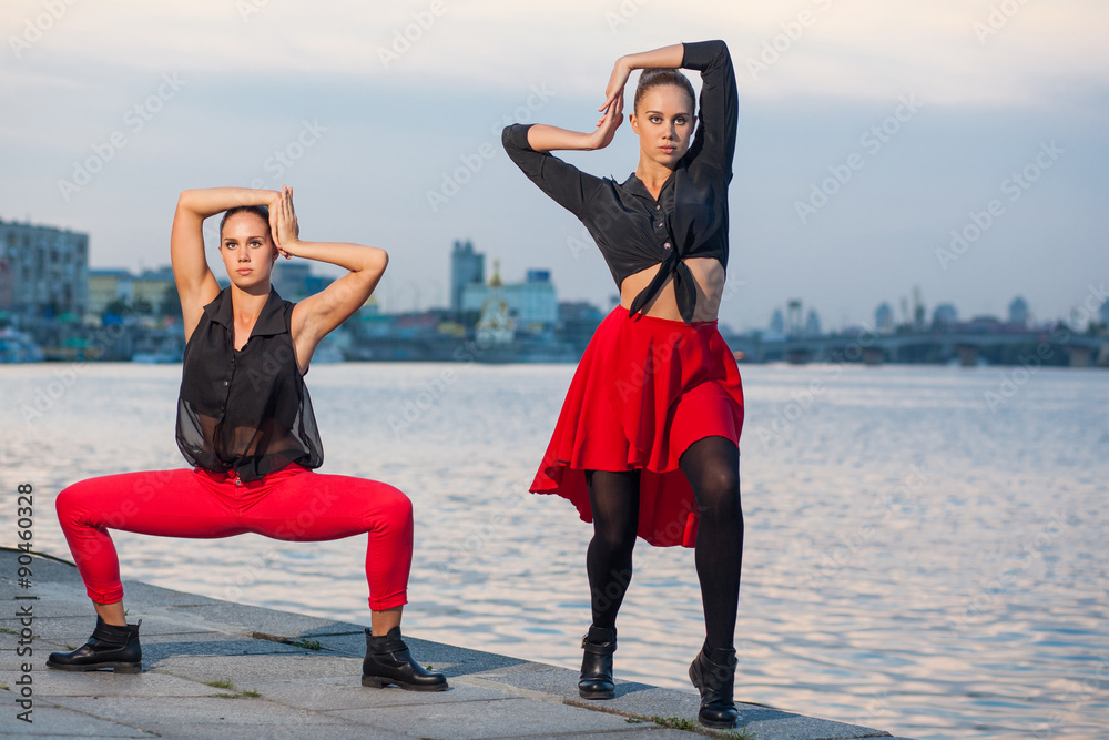 Two young beautiful twin sisters are dancing waacking dance in the city ...