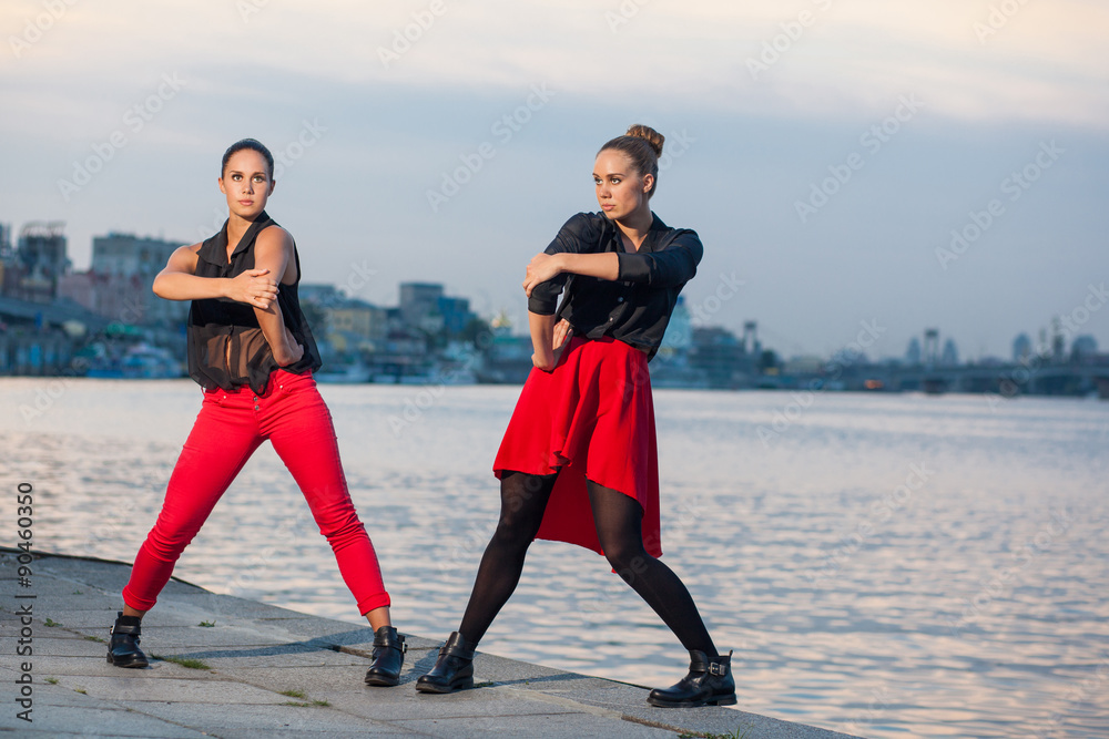 Two young beautiful twin sisters are dancing waacking dance in the city ...