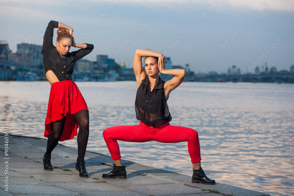 Two young beautiful twin sisters are dancing waacking dance in the city ...
