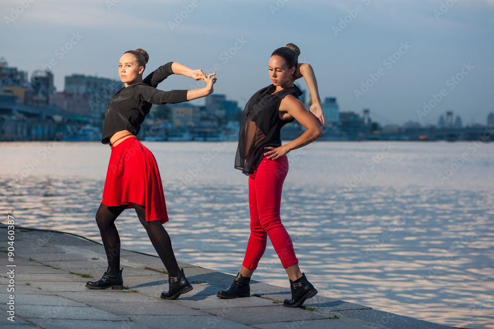 Two young beautiful twin sisters are dancing waacking dance in the city ...