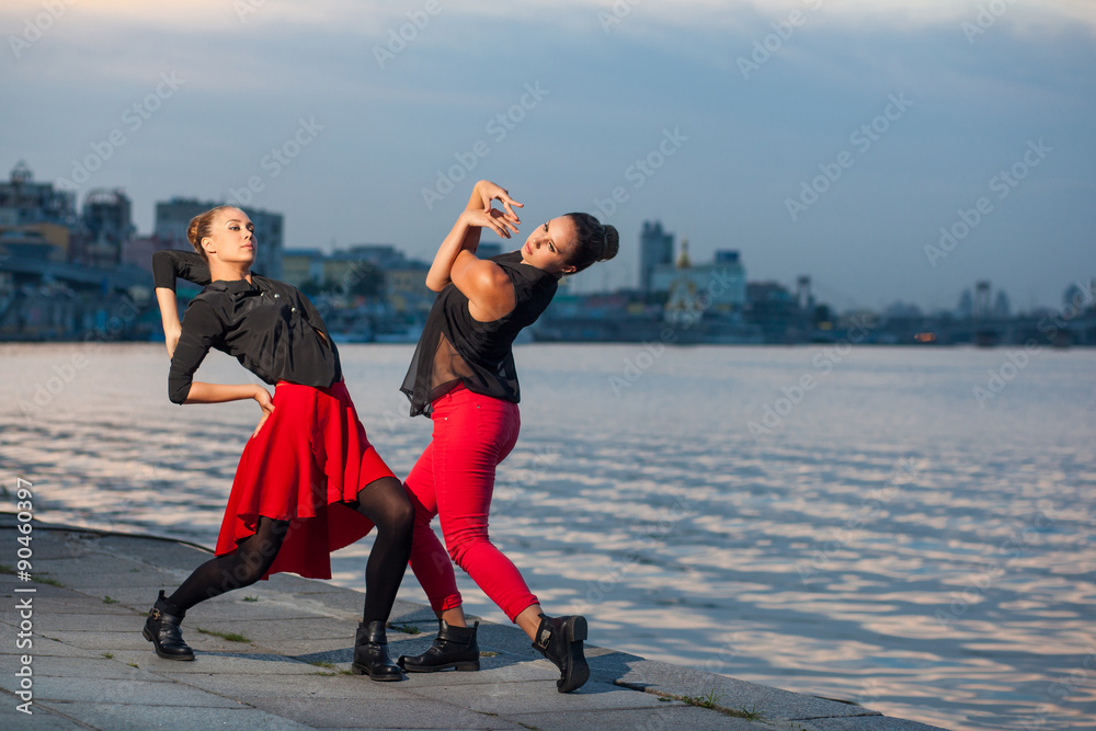 Two young beautiful twin sisters are dancing waacking dance in the city ...