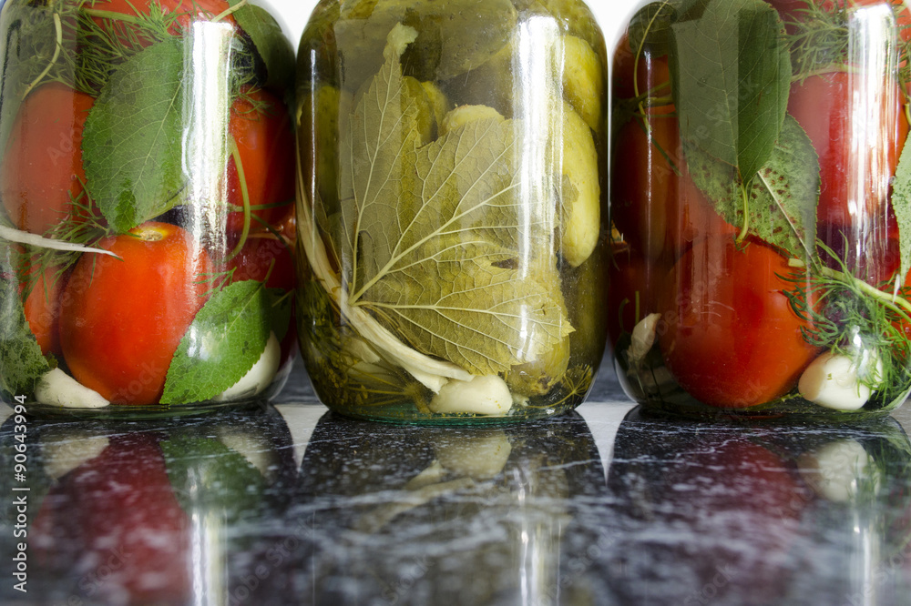 Canned vegetables on the marble table close-up. Tomatoes and cucumbers ...