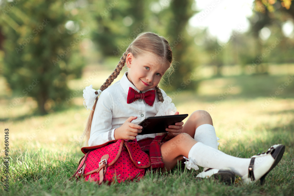 Foto de Funny kid girl 6-8 year old holding tablet outdoors. Looking at ...