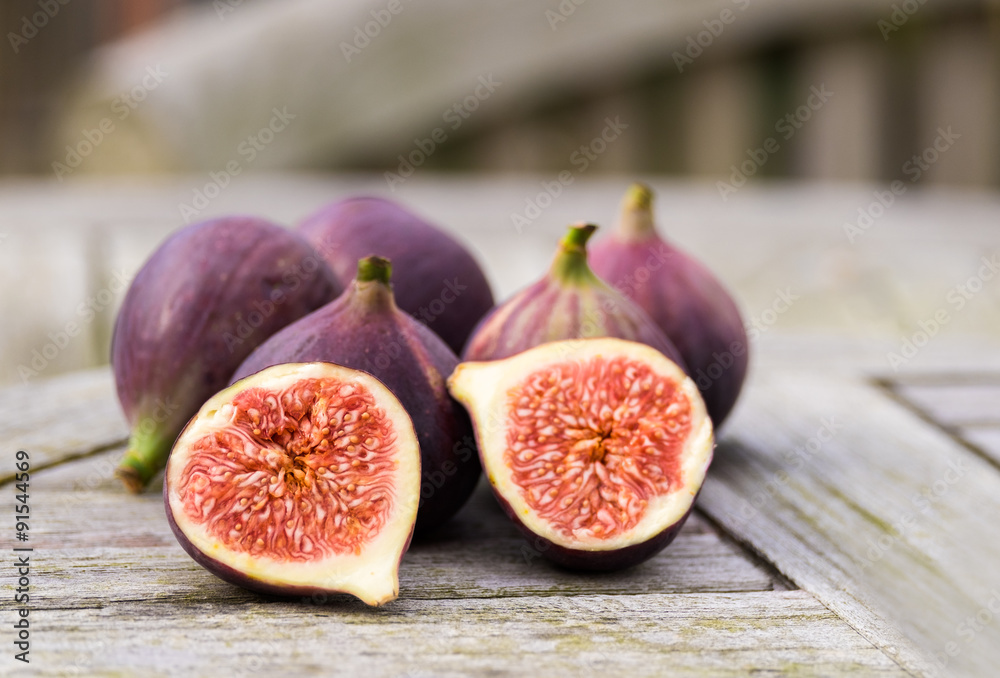 Whole figs and one fig sliced in half on top of a teak garden table ...