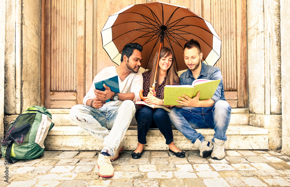 Three university students having fun reading books under umbrella ...