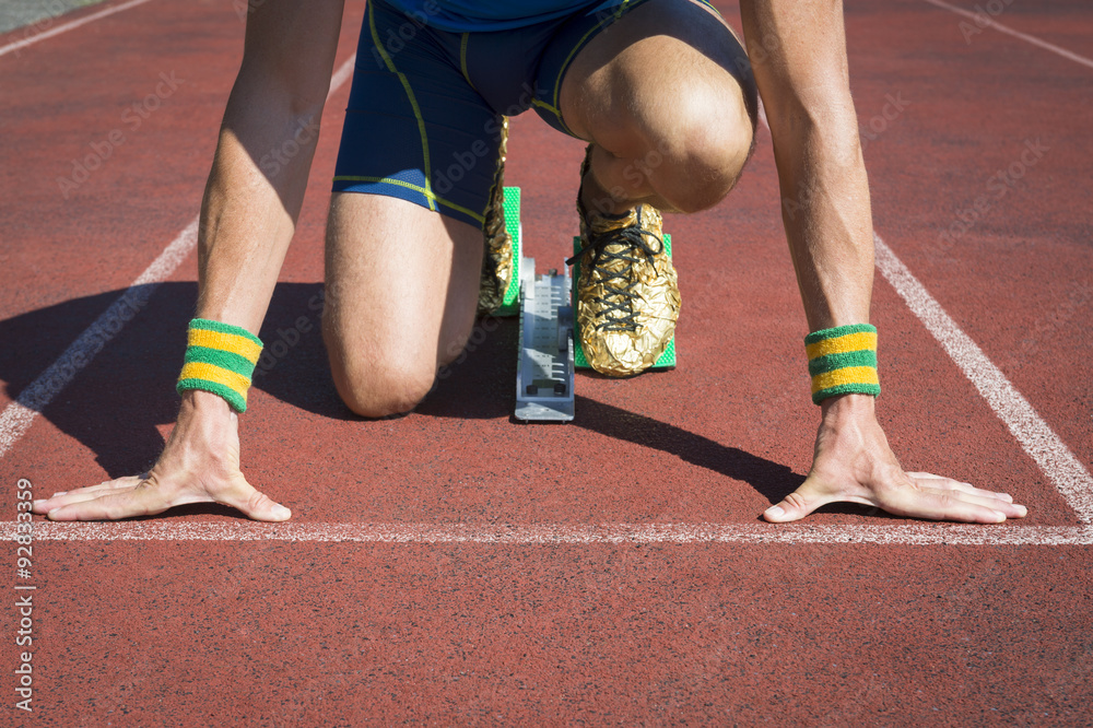 Athlete crouching at the starting line of a running track with gold ...
